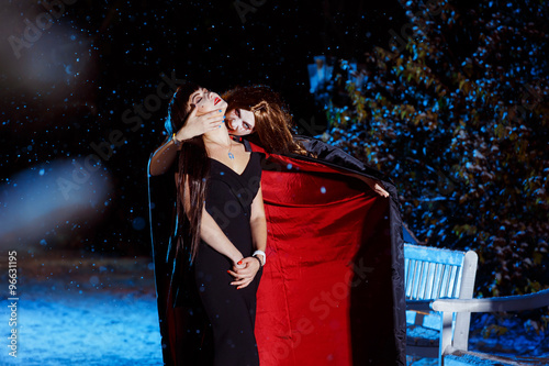 Beautiful Female Vampire In Long Pallium Is Biting Her Victim Stock
