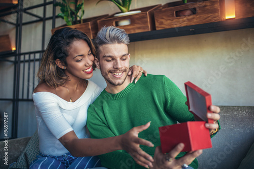 "Happy interracial couple sitting in cafe bar. Man giving gift to his ...